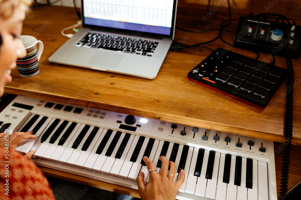 Music producer at home studio using keyboard controller from the back ...