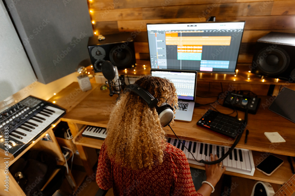 Music producer at home studio using keyboard controller from behind ...
