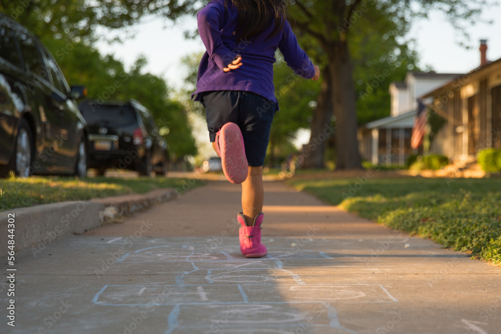 Girl hopping down hopscotch with one foot on a neighborhood sidewalk ...