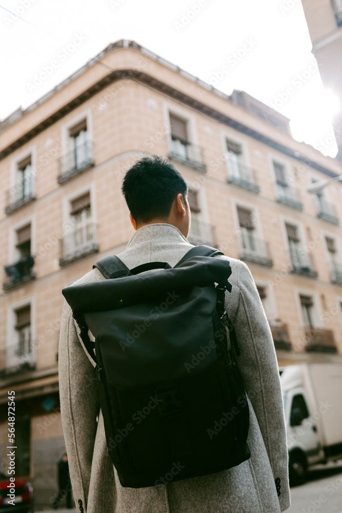 Back of young stylish man carrying a backpack in sunlight in the city ...