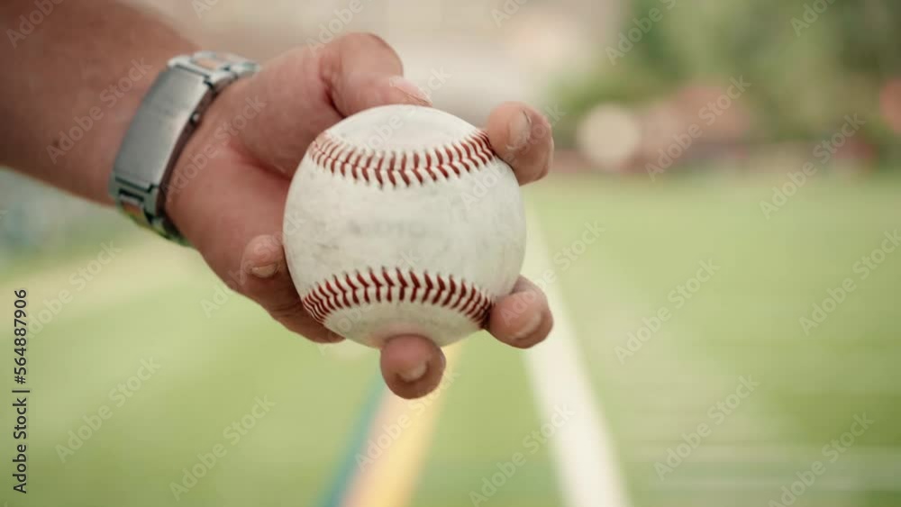 A male baseball hand rotates a ball in his fingers before pitching. The ...