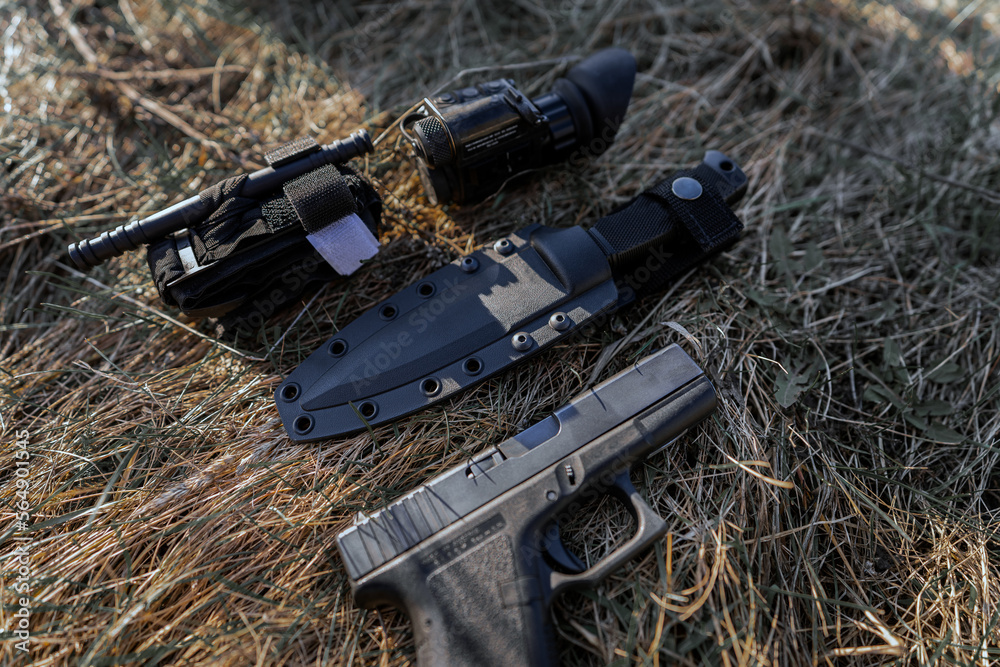 Foto de Tactical equipment on dry grass, a pistol, an army knife, a ...