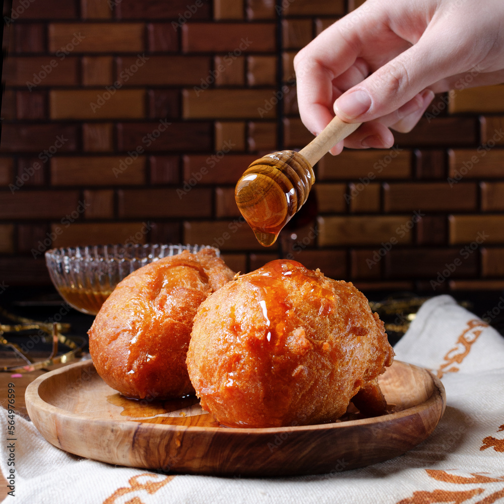 Hand holding a dipper of honey dripping on Italian Carnival fritters ...