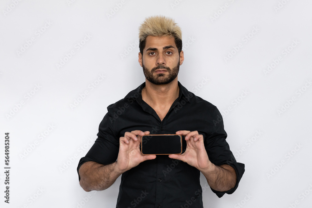 Serious young man presenting smartphone. Male Caucasian model with ...