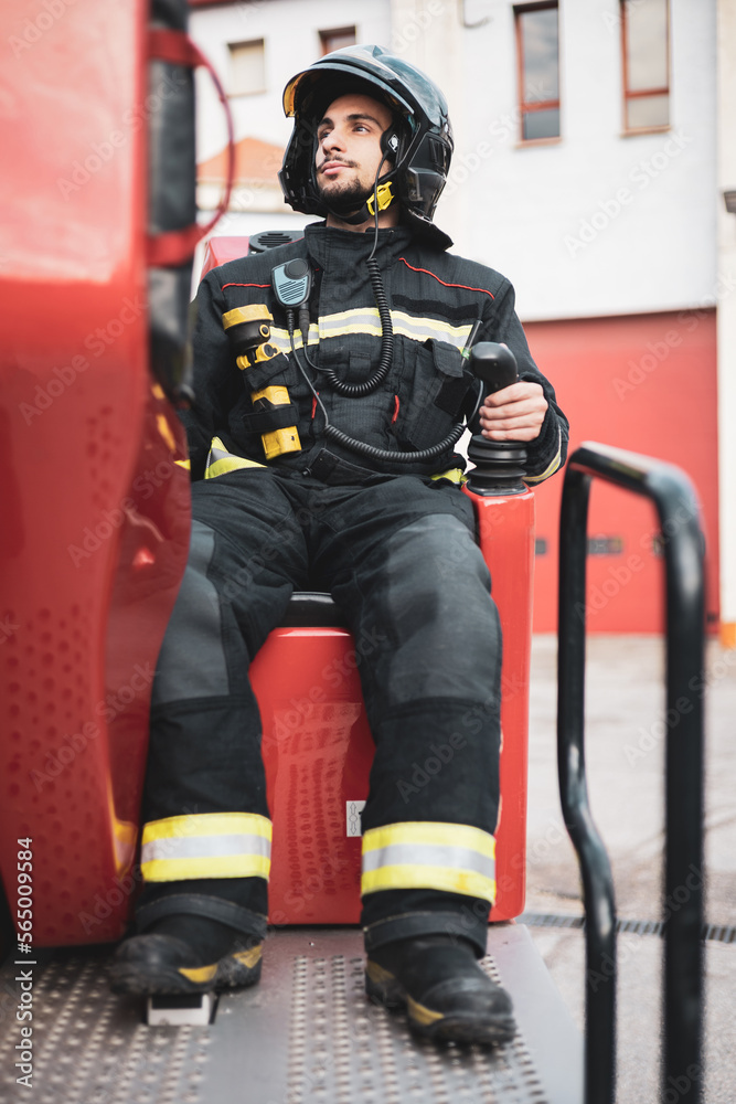 A uniformed firefighter sitting in the back of a crane truck using it ...