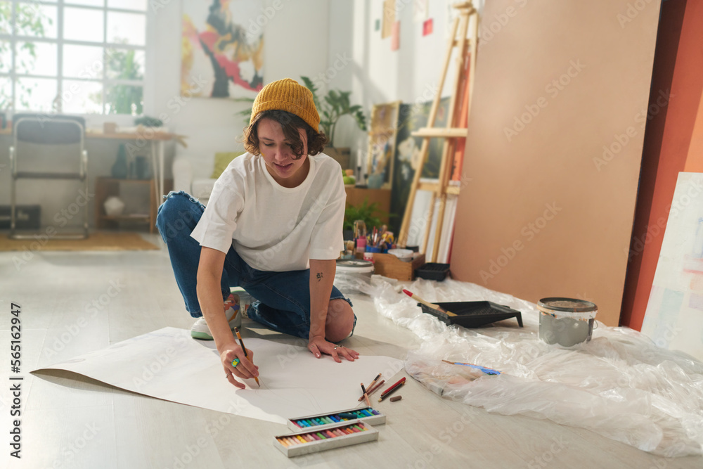 Pretty girl in casualwear sitting on the floor and drawing with crayons ...