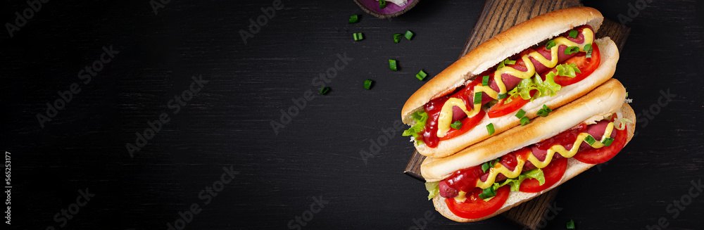 Hot dog with grilled sausage, tomato and lettuce on dark background ...