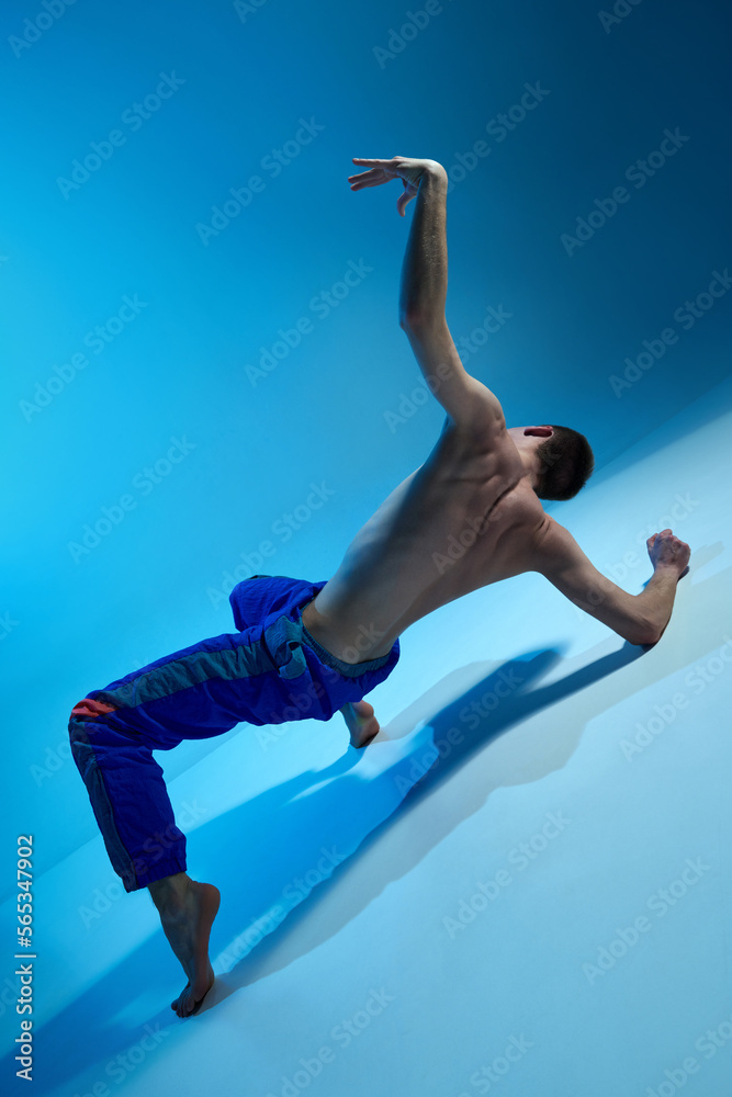 Contemporary dance style. Young shirtless man dancing over blue studio ...