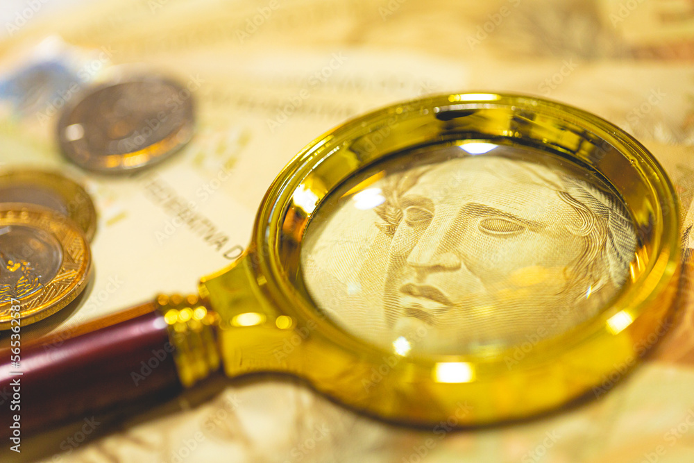 Notas do Real Brasileiro sobre uma mesa com uma lupa dourada na ...