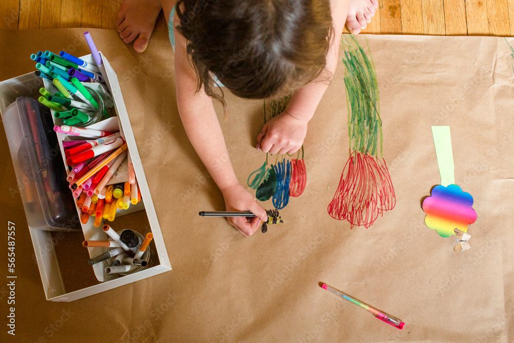Above-view of a small child drawing a large mural of colorful flowers ...
