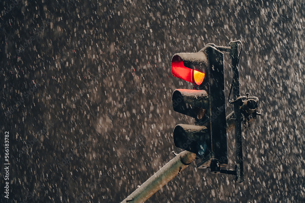 Red traffic light on a pole during a winter night with massive snowfall ...