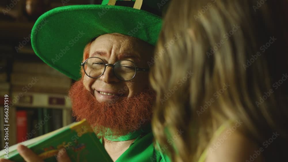 Old leprechaun is reading book , telling fairy tale story for little ...