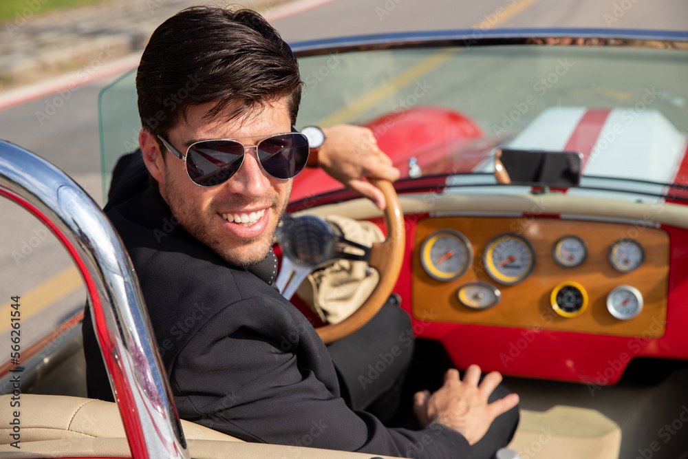 young man in convertible car looking at camera, smiling, man wears suit ...
