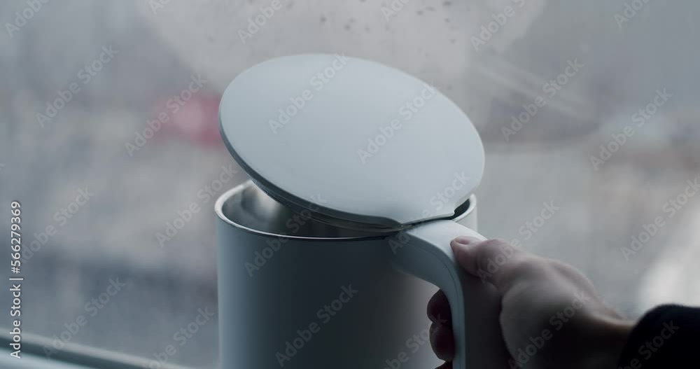 The kettle creates steam, boiled water. The man's hand opens the lid ...