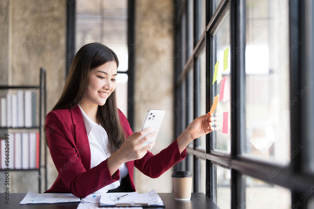 Young smiley attractive, businesswoman using sticky notes in glass wall ...