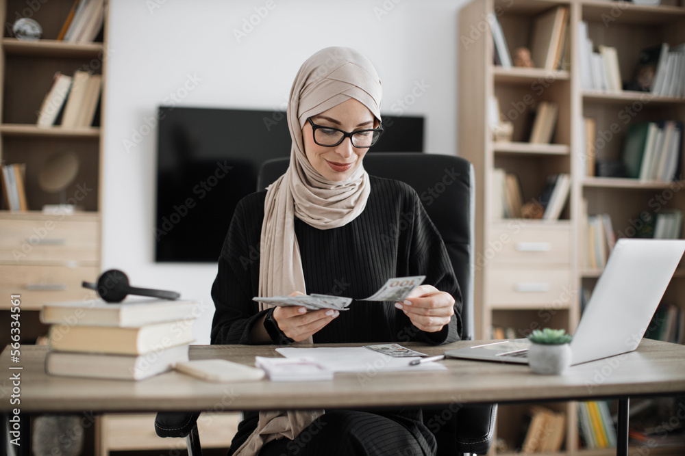 Rich muslim business woman working on laptop counting money cash ...
