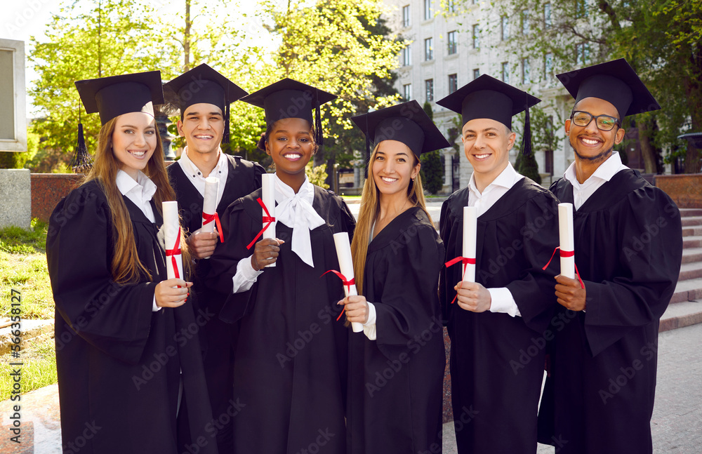 Group portrait of happy diverse university graduates in green campus ...