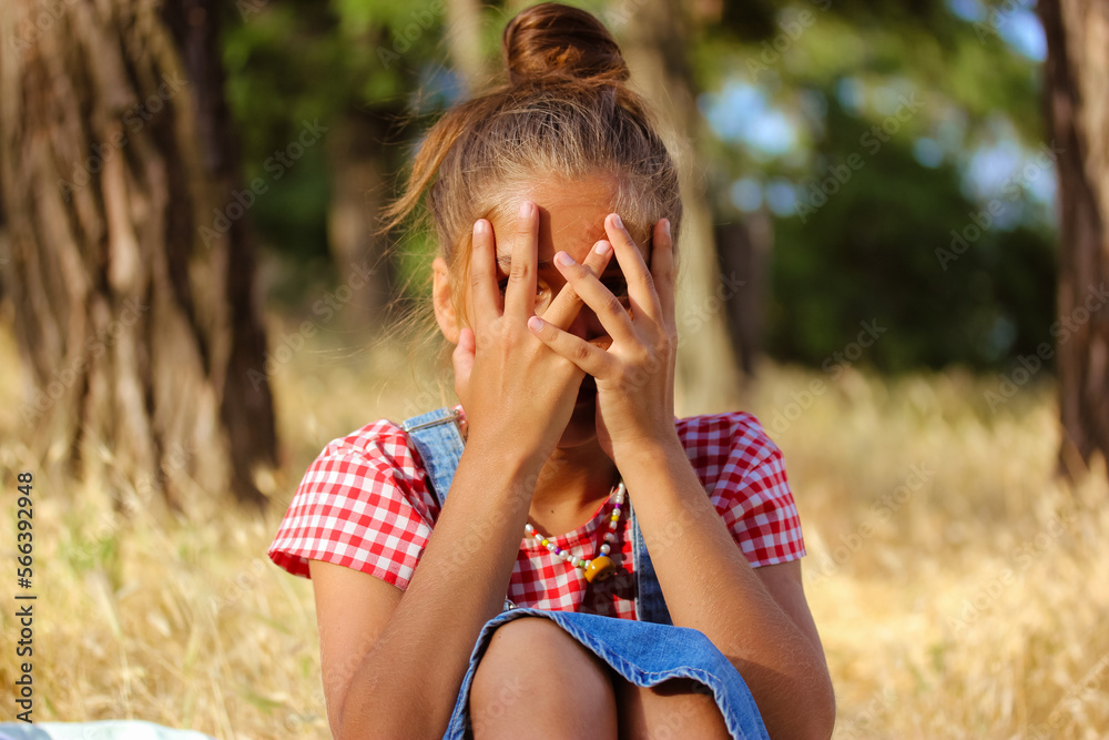 Little girl hiding face portrait. A kid in denim sundress sits in a ...