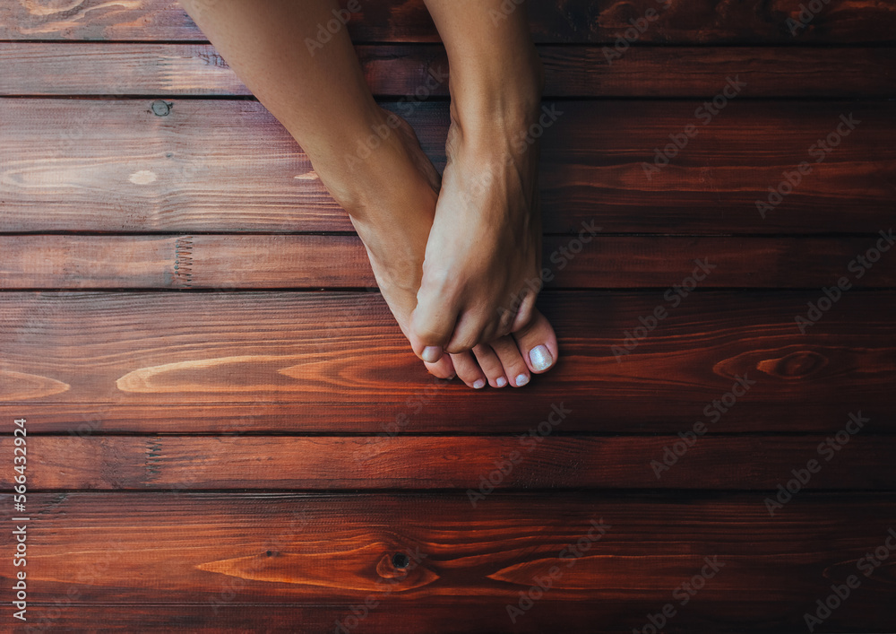 Female feet on a brown wooden floor background close up. Itching and ...
