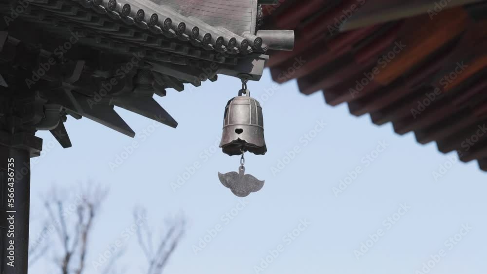 Close up of bronze bell swaying in wind with temple buildings ...