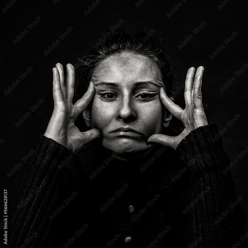 Conceptual dark portrait of woman stretching the skin of her face in ...