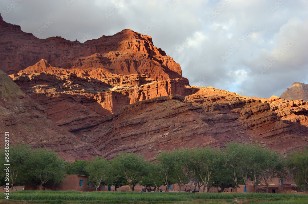 Red bluffs and cliffs tower over the trees of an orchard, on the edge ...