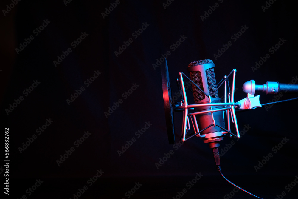 a black microphone on black background under the neon light. podcasting ...
