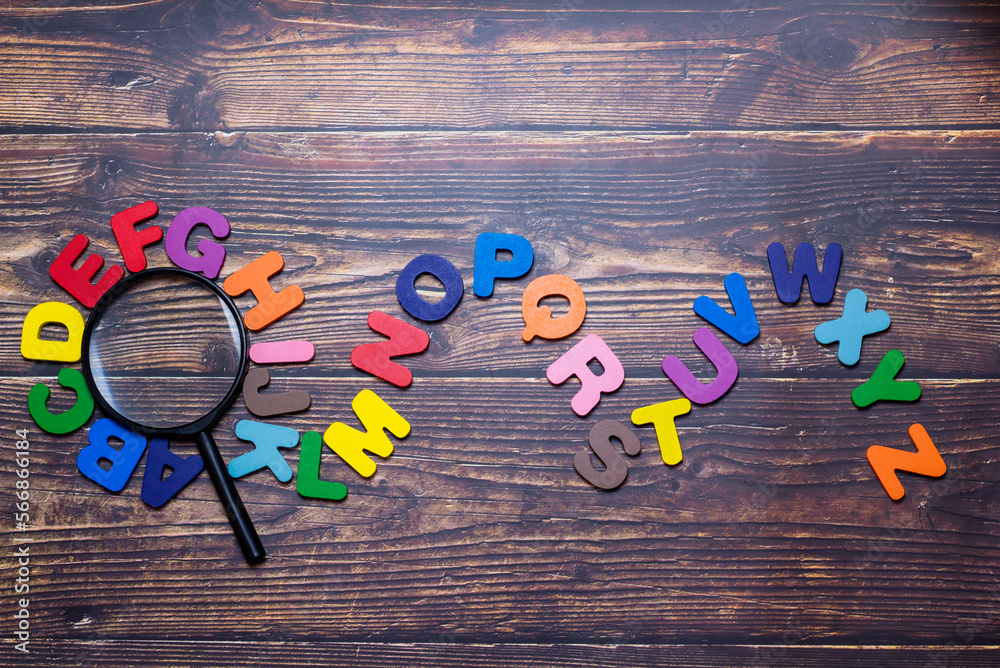 Multicolored English letters spread on the wooden floor. Magnifier and ...