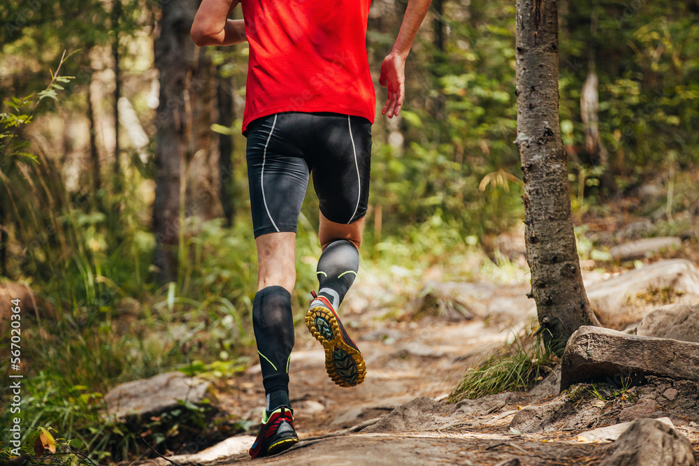 male runner in compression calf sleeve running forest trail Stock Photo ...
