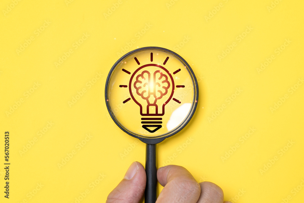 Hand holding magnifier glass inside of drawing of glowing light bulb ...