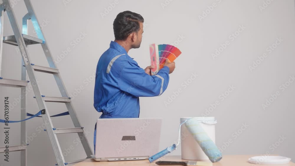Confused painter checking colour on laptop by holding colour chart at ...