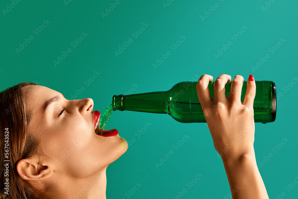 Woman pouring green beer into her mouth over green studio background ...