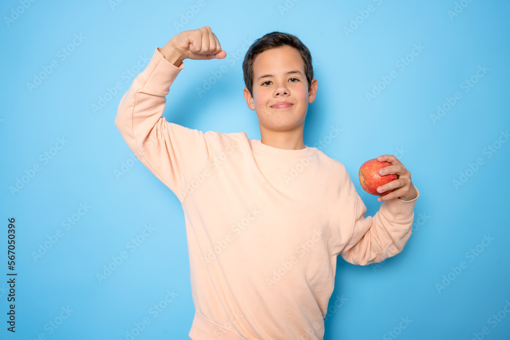 child on blue background eating the green apple he holds in one hand ...