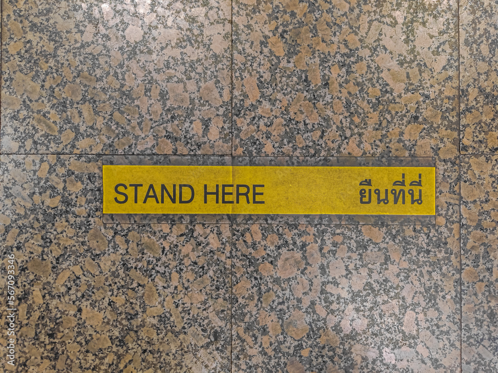 Stand here sign on the floor showing where to stand in English and Thai ...