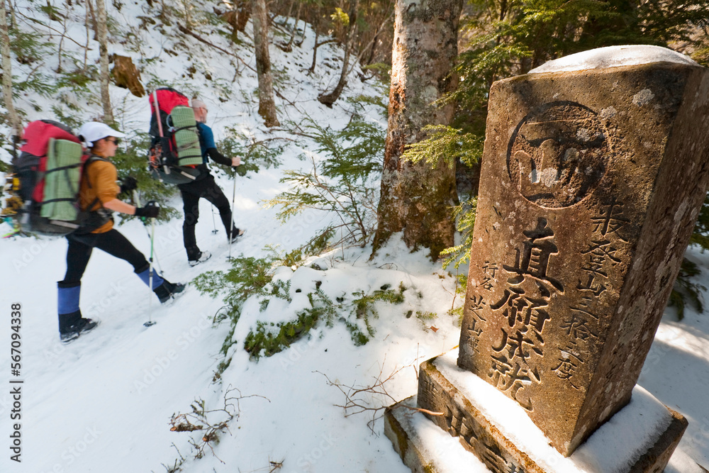 Two people are hiking on a trail next to a pillar with Japanese ...