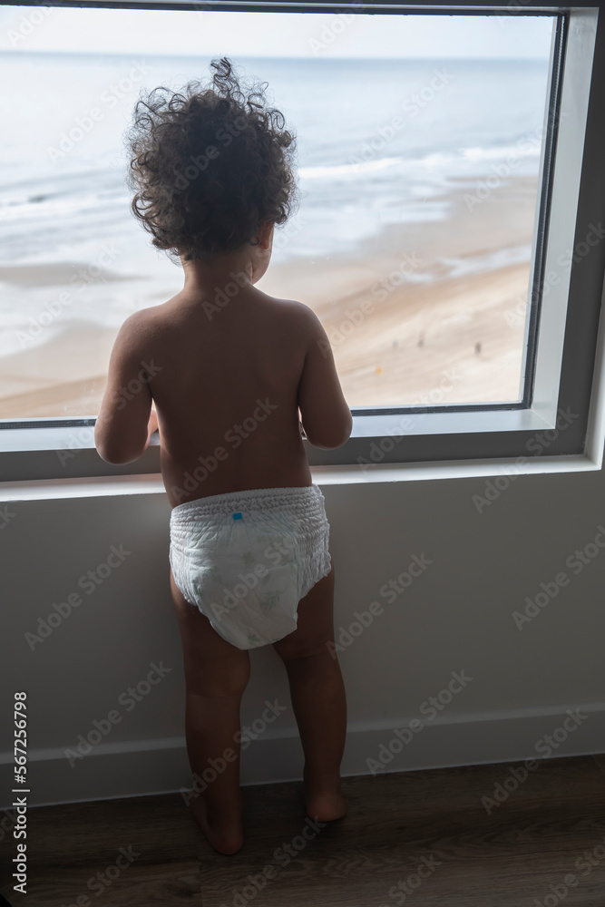 Cute boy toddler on summer vacation looking out of the hotel window at ...