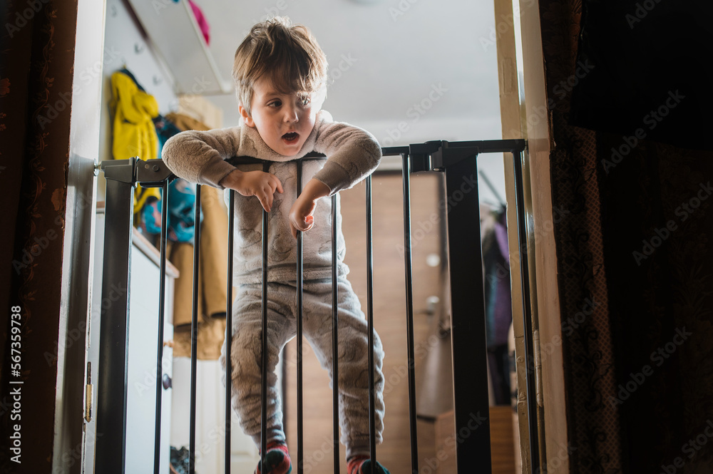 Toddler tries open lock on child safety gate. The child plays behind ...