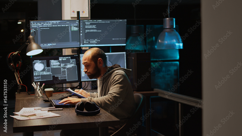 IT web developer comparing data files on clipboard papers and multiple monitors to program new ...