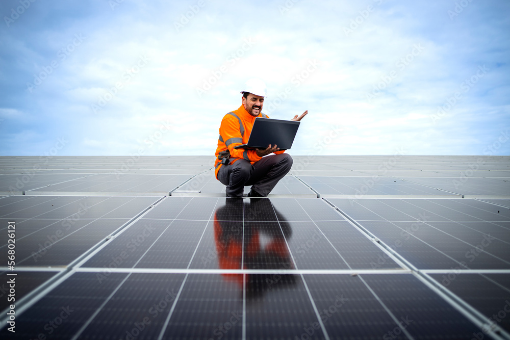 Happy solar panel worker using laptop computer and checking electricity ...