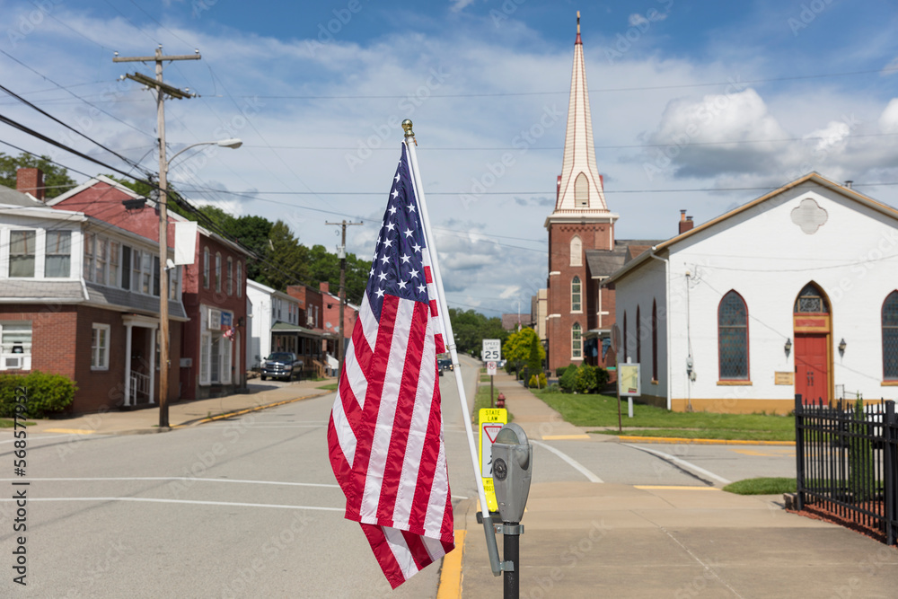 American flag flying on a quiet main street with houses and a church ...