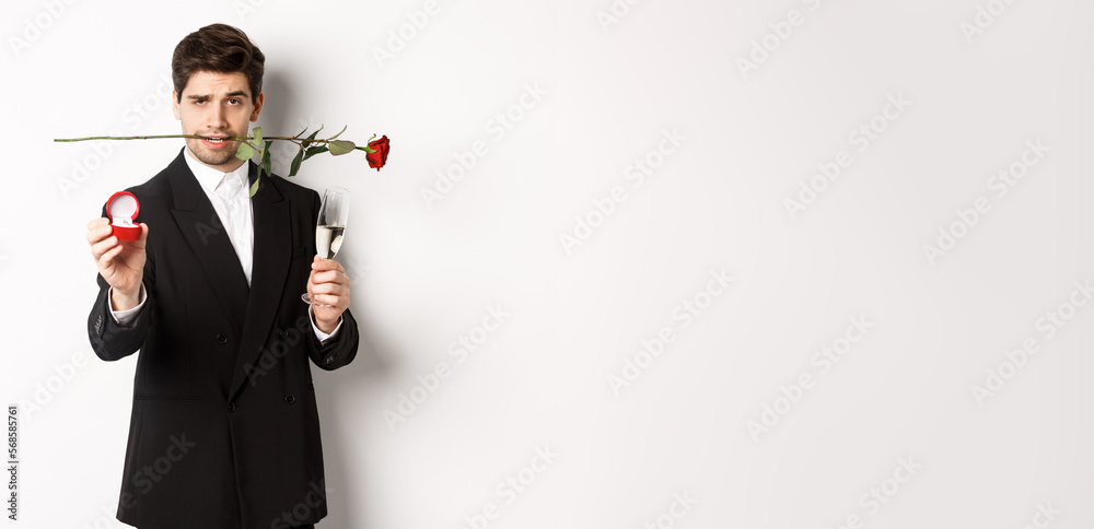 Passionate young man in suit making a proposal, holding rose in teeth ...