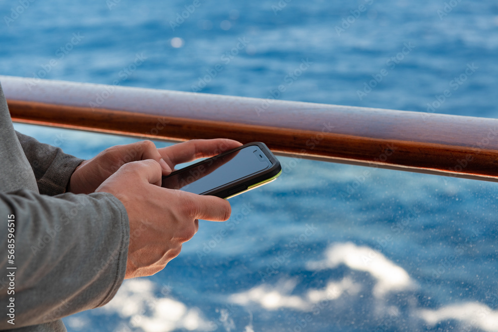 Hand of man using mobile smart cell phone on a ship with the blue ocean ...