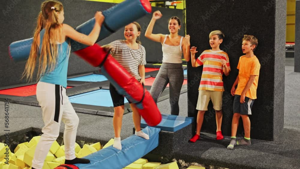 Cheerful teen girl doing funny fighting by pugil sticks on battle beam ...