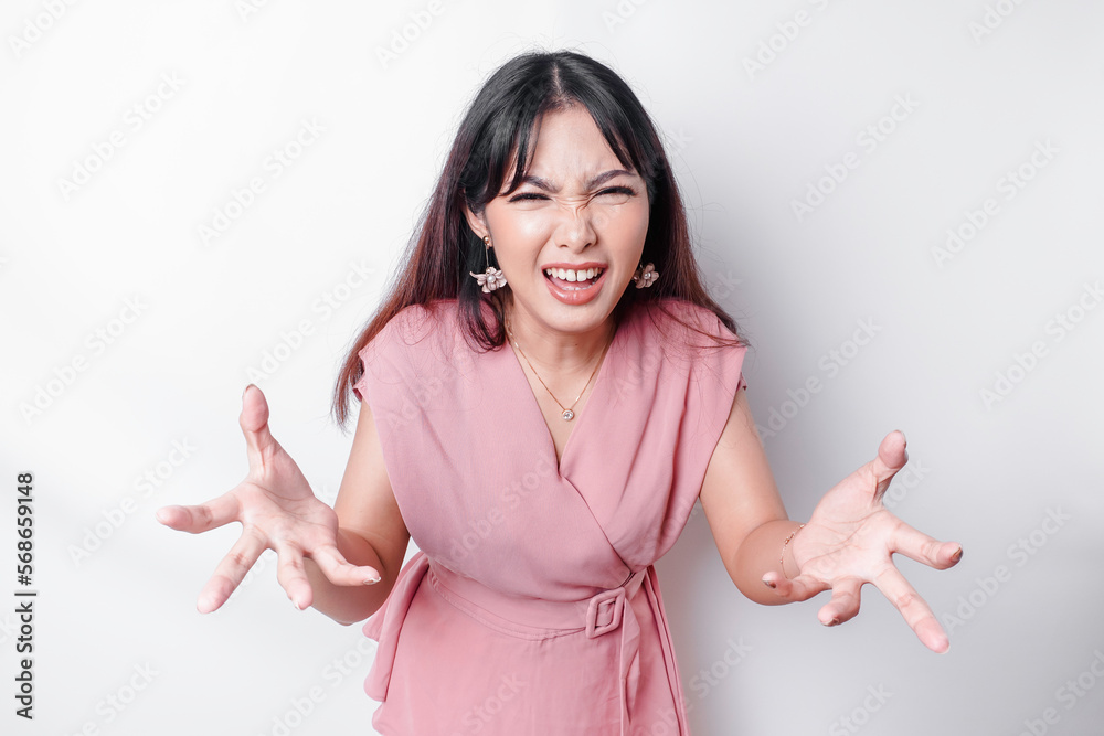 A dissatisfied young Asian woman looks at the camera posing on a white ...