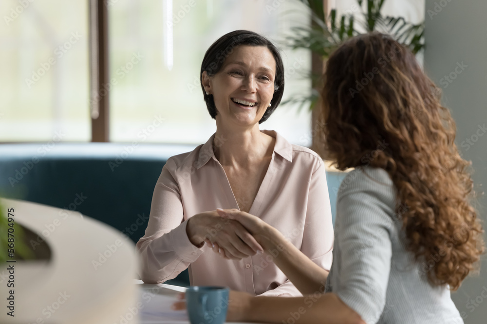 Positive senior business woman giving handshake to younger colleague at ...