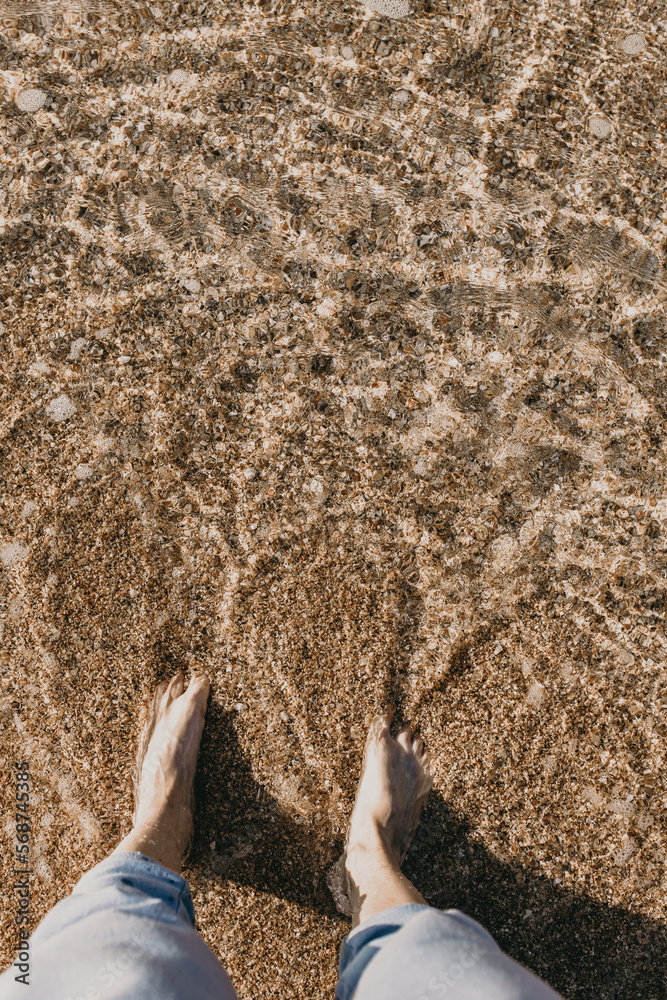 Poster Upper view of male or female feet standing on beach in pure ...