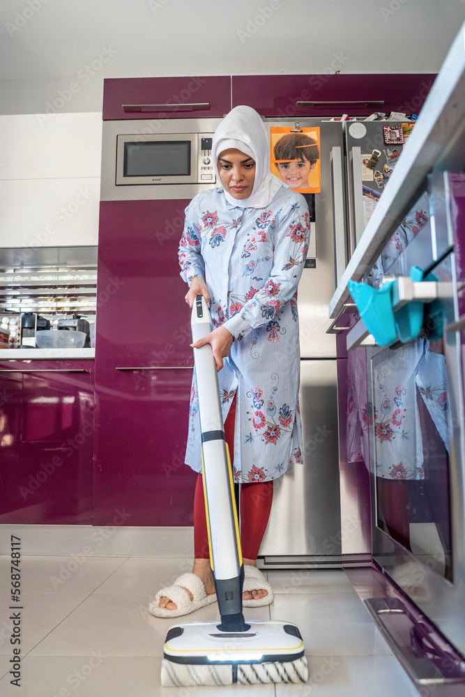 Middle-aged muslim woman vacuum with wireless cleaner Kitchen floor ...