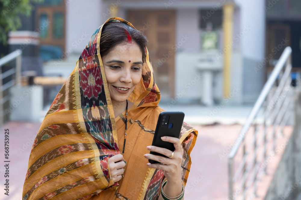Indian rural woman in traditional saree and using smartphone at home ...