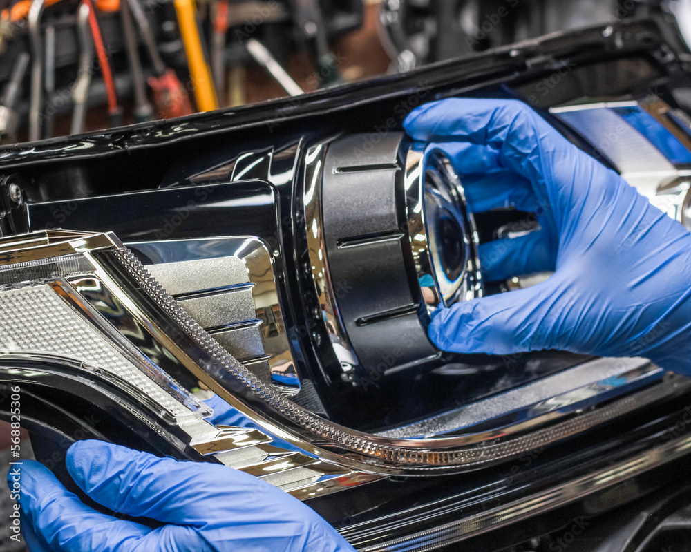 Car headlight in repair close-up. An auto mechanic wearing gloves ...