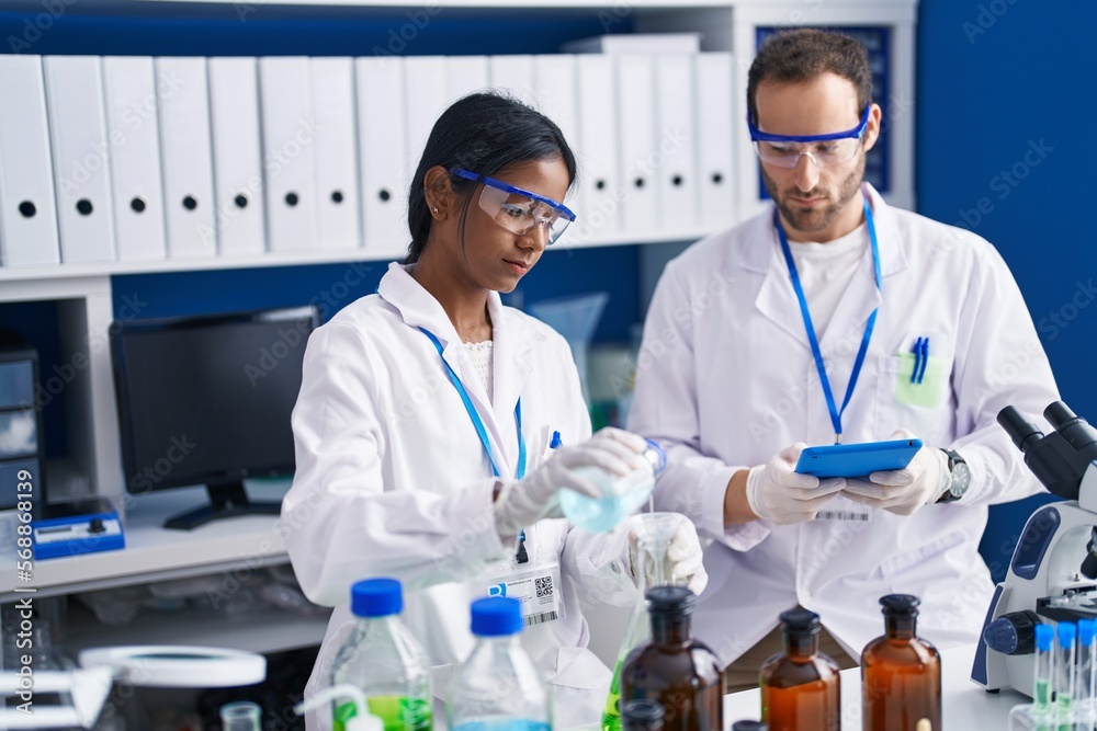 Man and woman scientists using touchpad measuring liquid at laboratory ...
